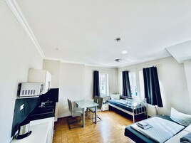 Quarto de hotel com cama, escrivaninha, cadeira, mesinha e janela com cortinas.