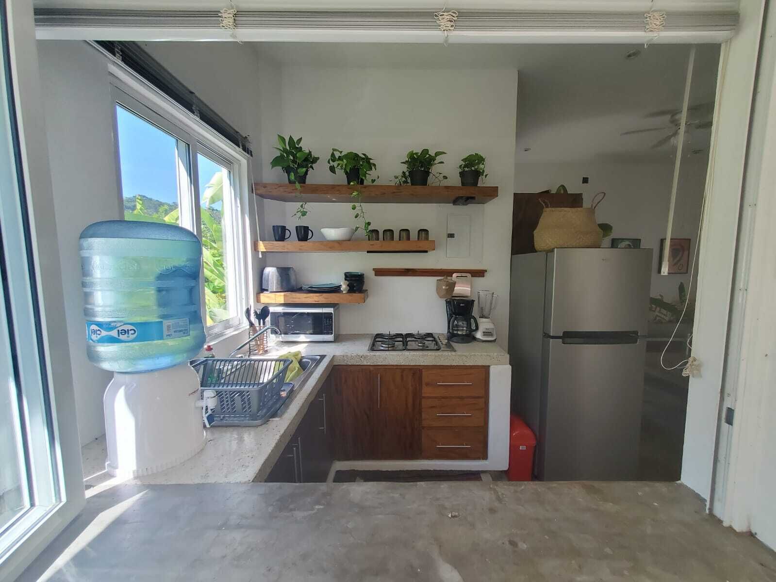 Cozinha compacta equipada com dispenser de água, micro-ondas, fogão a gás e geladeira.