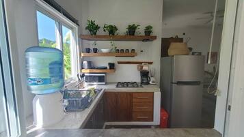 Cozinha compacta equipada com dispenser de água, micro-ondas, fogão a gás e geladeira.