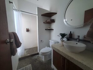 Casa de banho com sanita, lavatório e área de duche.