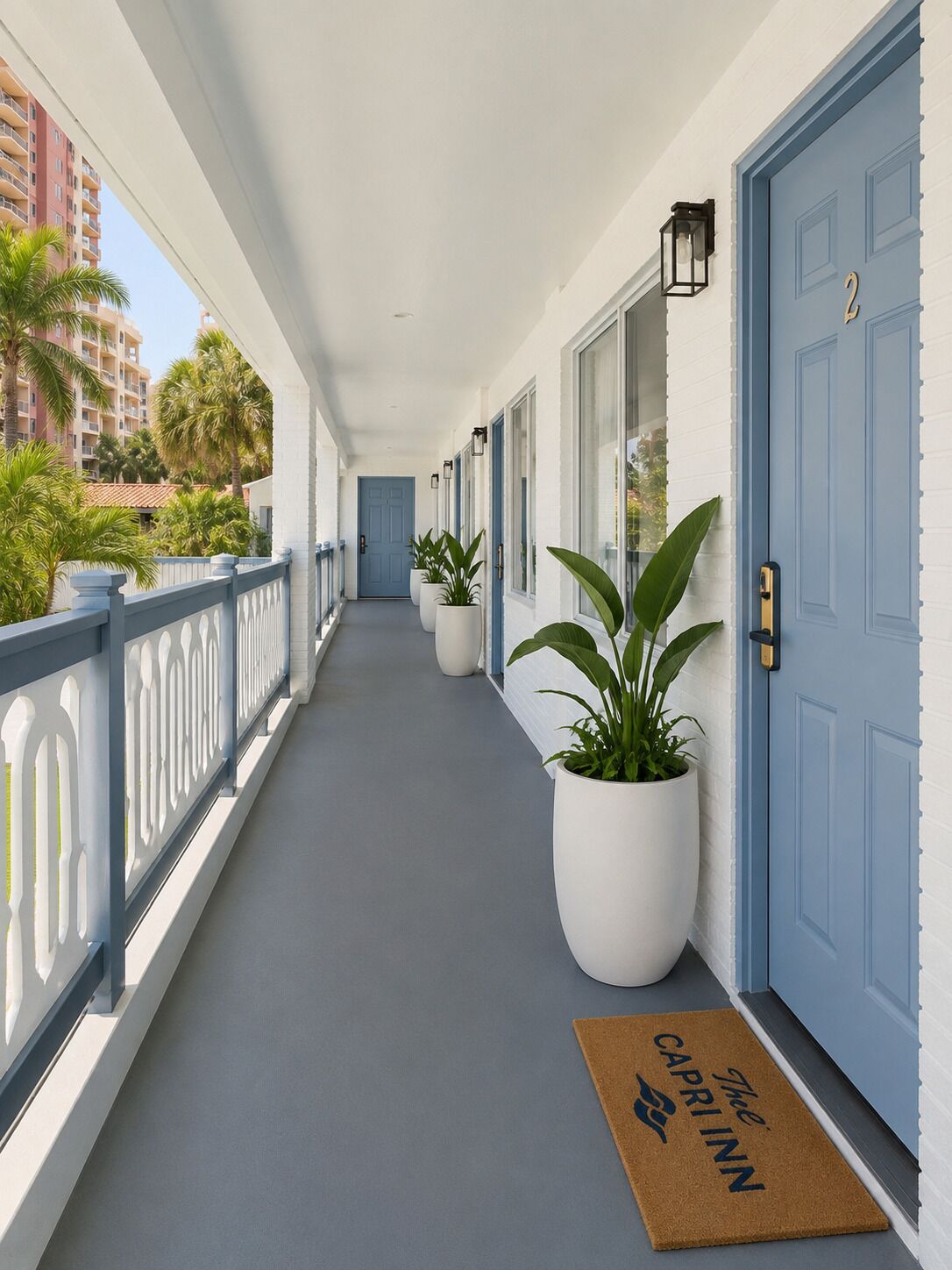 Corredor coberto com porta azul, plantas em vasos e tapete de entrada.