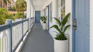 Corredor coberto com porta azul, plantas em vasos e tapete de entrada.