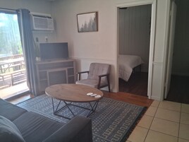 Quarto com televisão em suporte, cadeira, cama e mesa com tapete.