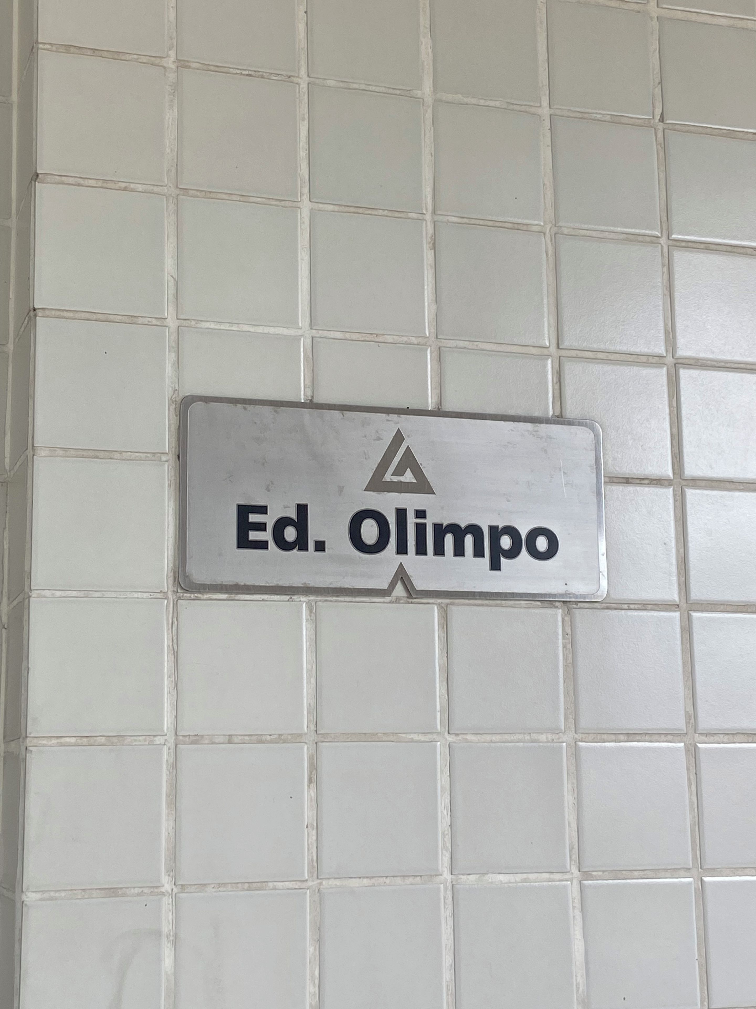 Placa com o nome 'Ed. Olimpo' em uma parede de azulejos.
