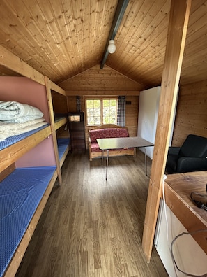 Interior de cabana com beliches, mesa e janela com cortinas.