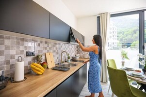 Cozinha moderna com armários escuros, bancada de madeira e vista para um edifício por uma janela grande.