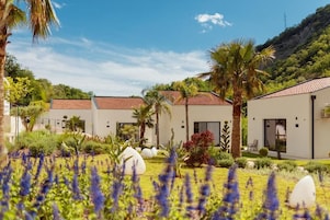 Hotel moderno com vários quartos, jardim bem cuidado com diversas plantas e montanhas ao fundo.