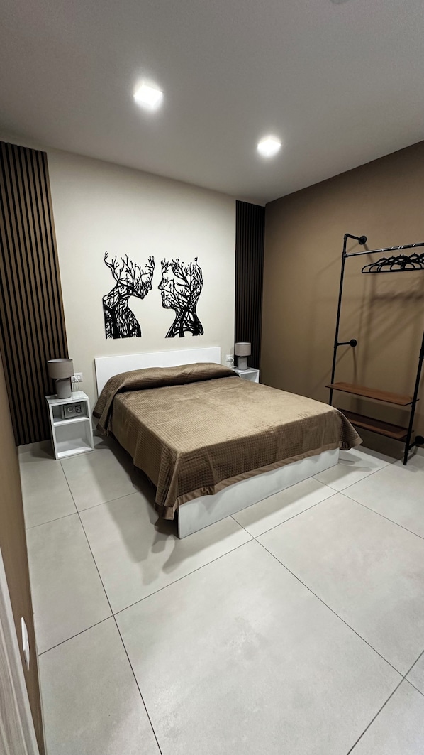 Quarto moderno com cama grande, obra de arte na parede, mesa de cabeceira com abajur e um cabideiro.