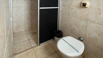 Casa de banho com sanita, um caixote de lixo preto e cabine de duche.