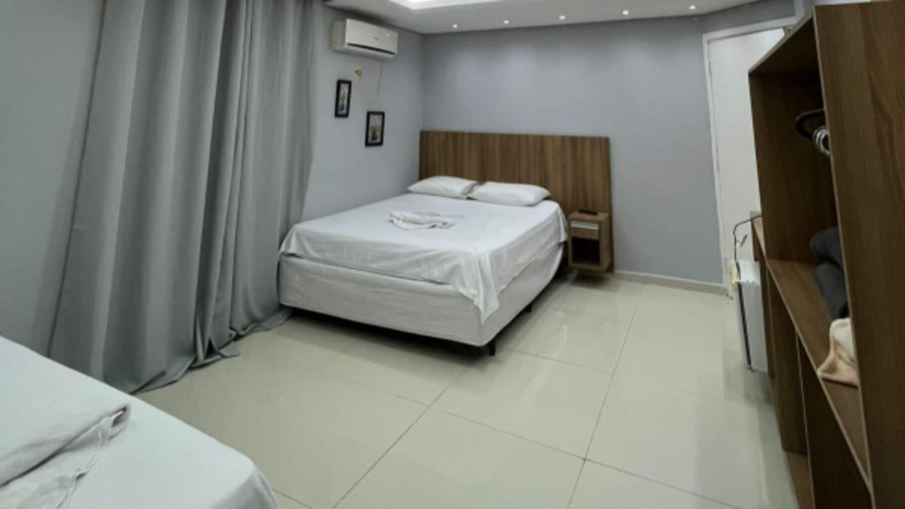 Quarto com cama, mesa de cabeceira, guarda-roupa e ar condicionado na parede.