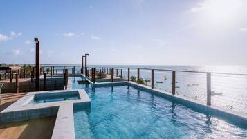 Piscina com vista para o mar, rodeada por um deck de madeira e guarda-corpo de metal.