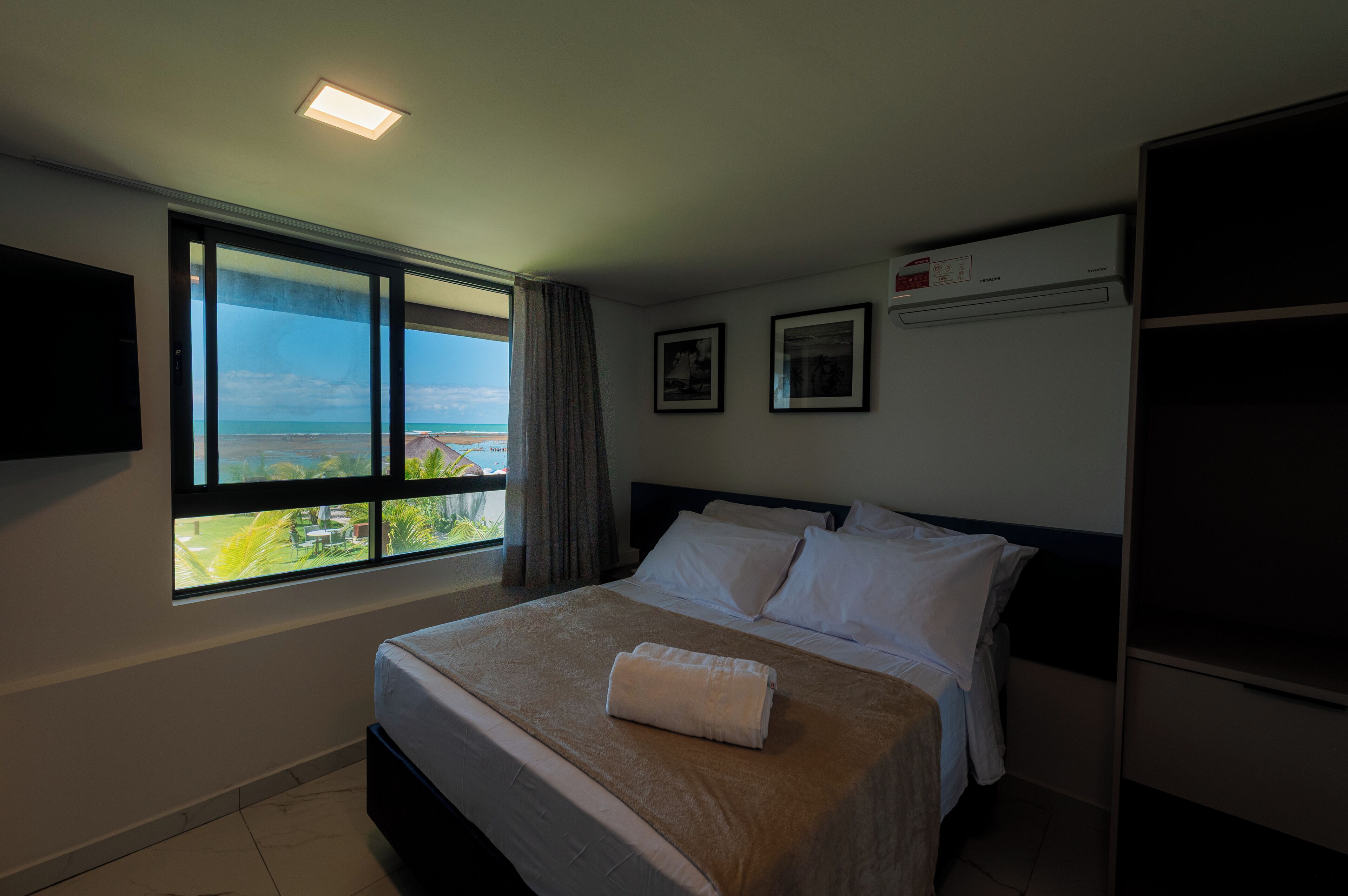 Quarto de hotel com cama, janela grande com vista, televisão de tela plana e ar condicionado.