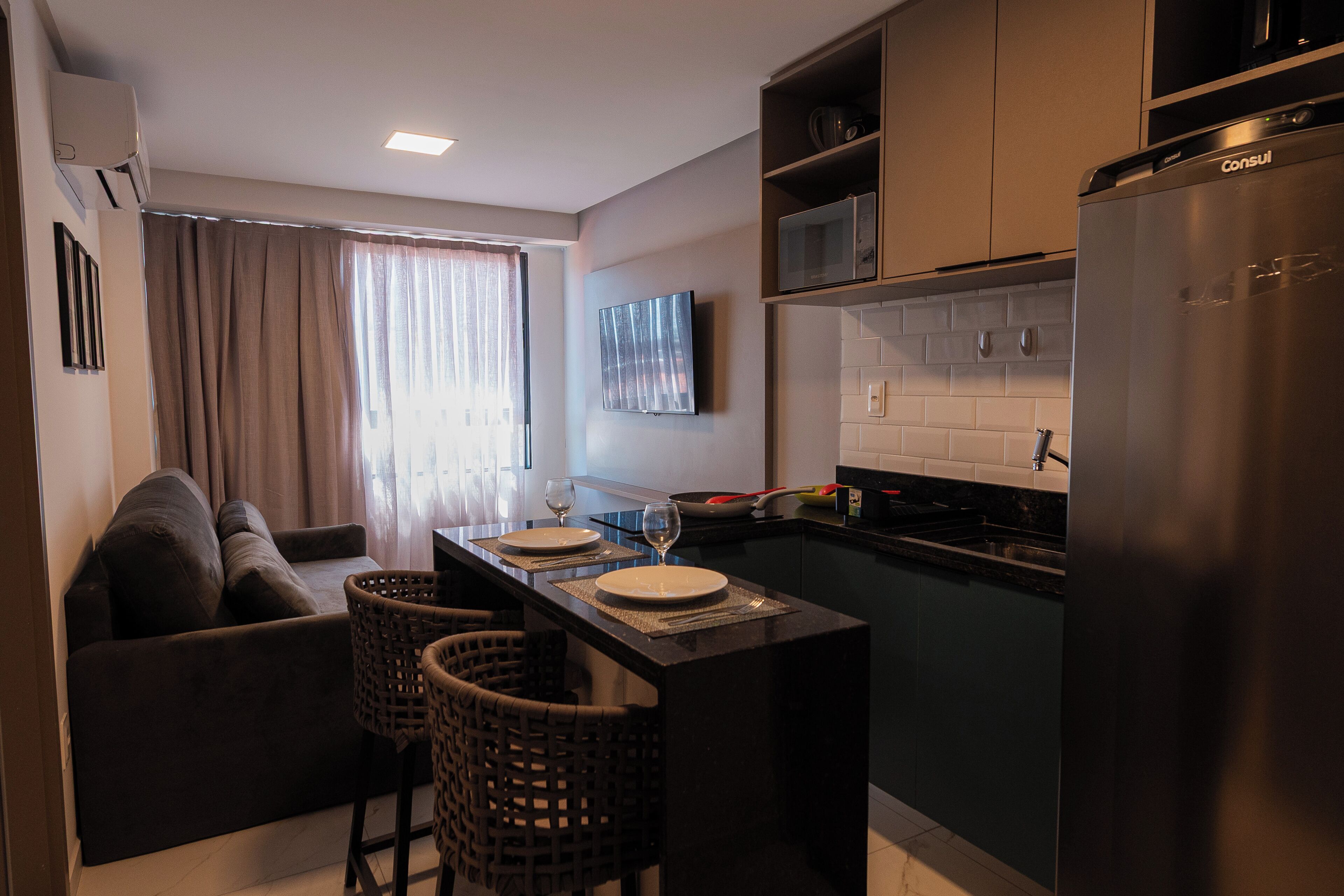 Cozinha compacta com área de refeições, televisão integrada e geladeira.