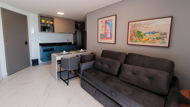Uma sala de estar moderna com sofá, área de refeições com mesa e cadeiras, e cozinha com armários e eletrodomésticos.