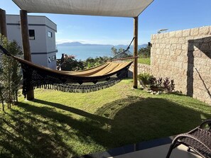 Uma rede sob área sombreada, vista para o mar e montanhas.