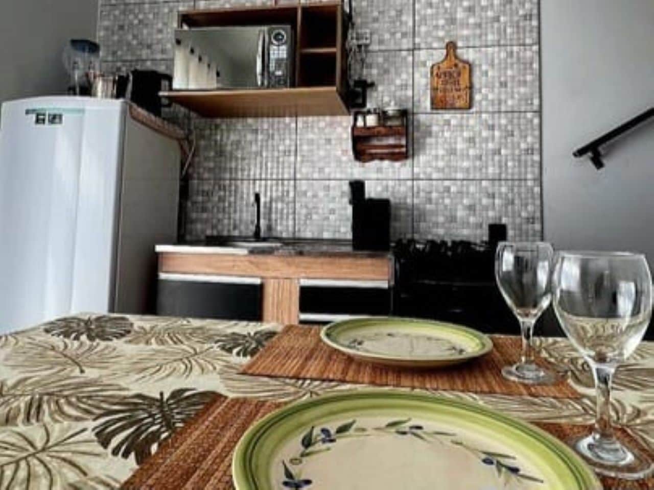 Cozinha com geladeira, micro-ondas e prateleira com utensílios de cozinha.