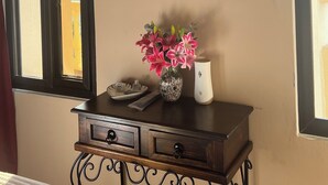 Quarto com cama, televisão de tela plana na parede, pequena mesa de madeira com um vaso de flores e janela com cortinas.
