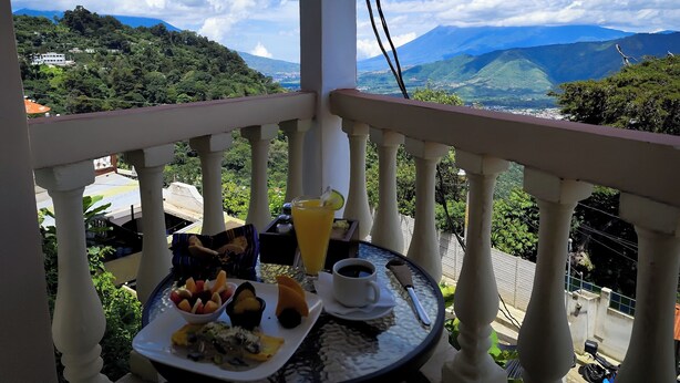 Varanda com mesa posta para o café da manhã, com vista para uma paisagem montanhosa.