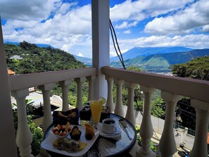 Varanda com mesa posta para o café da manhã, com vista para uma paisagem montanhosa.