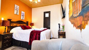 Quarto de hotel com cama, mesas de cabeceira, luminária, um quadro na parede e uma porta.