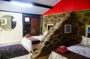Quarto com duas camas, parede de pedra, espelho e porta para o exterior.