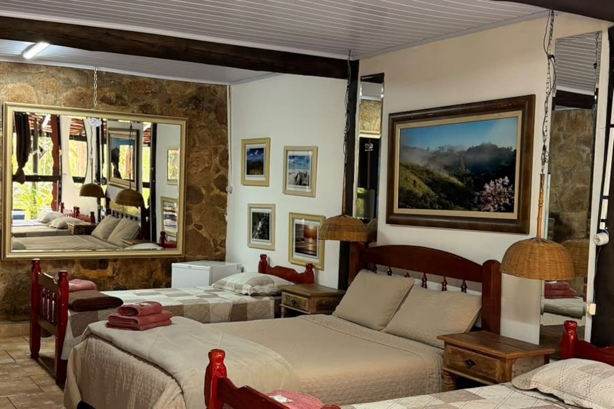 Quarto com duas camas, parede de pedra, espelho grande e um quadro.