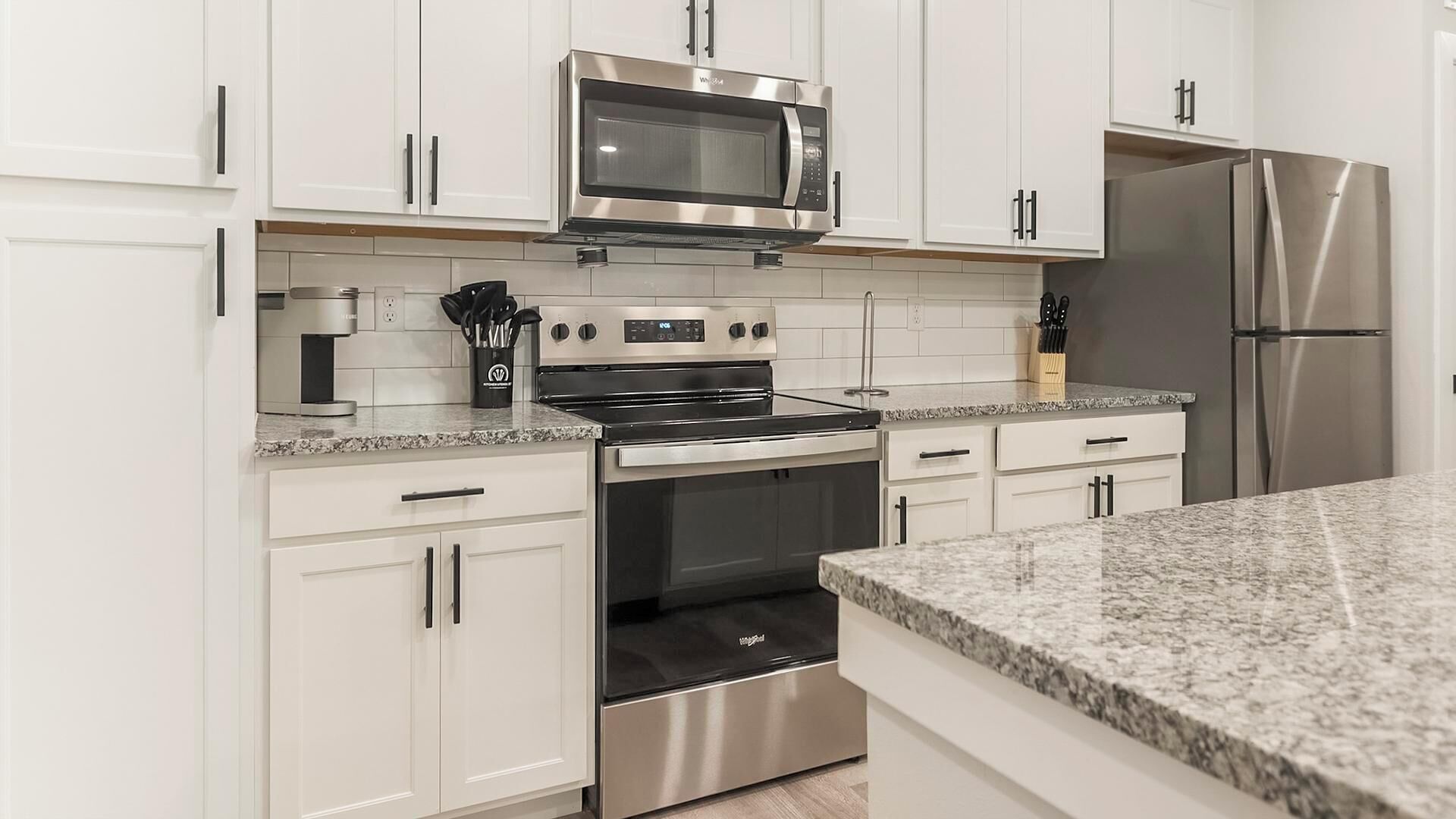 Uma cozinha moderna com armários brancos, eletrodomésticos de aço inoxidável e bancadas de granito.
