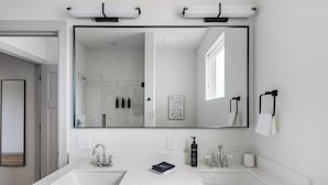 Casa de banho moderna com duas lavatórios, um espelho grande e um chuveiro visível no reflexo.