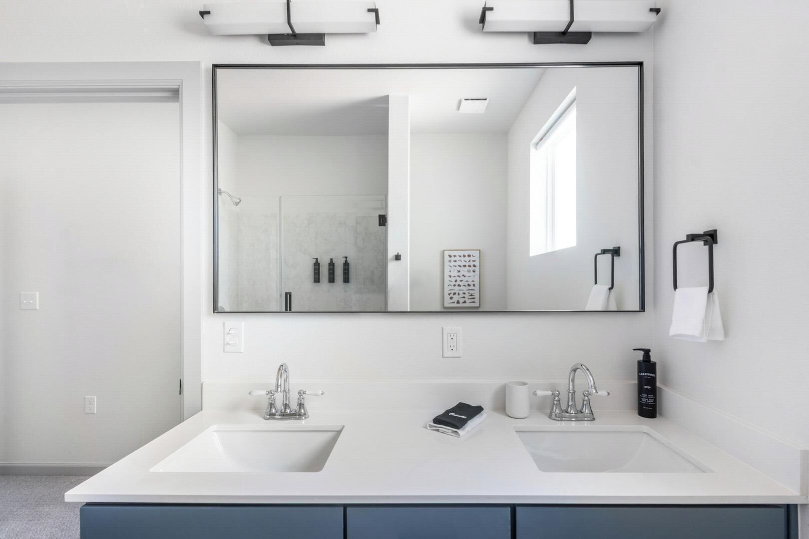 Uma casa de banho moderna com duas pias, um espelho grande e um porta-toalhas.