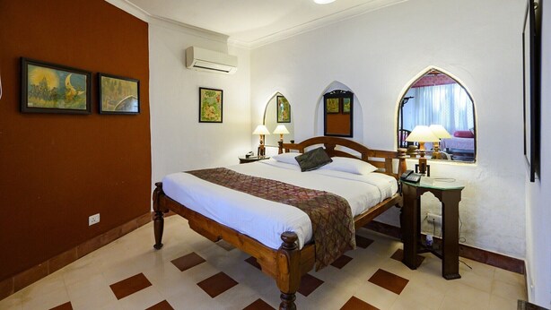 Quarto de hotel com cama de madeira, mesa de cabeceira com luminárias, espelho e janela com cortinas.