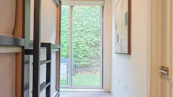 Um corredor com piso de madeira, uma porta de vidro deslizante que dá para um jardim e um quadro na parede.