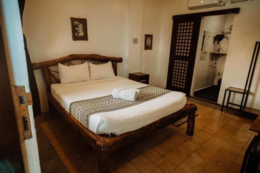 Uma cama de madeira com colchão e travesseiros brancos, cabeceira de madeira e colcha estampada.