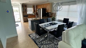 Uma sala de estar ampla com uma mesa de jantar, cadeiras pretas, um sofá branco e um tapete estampado.