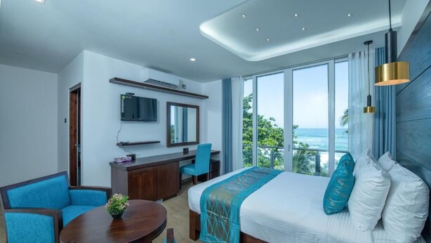 Quarto de hotel com cama, escrivaninha, cadeira, televisão e vista para o oceano.