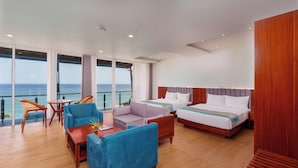 Quarto de hotel com uma janela grande, duas camas, um espaço de estar com cadeiras e piso de madeira.