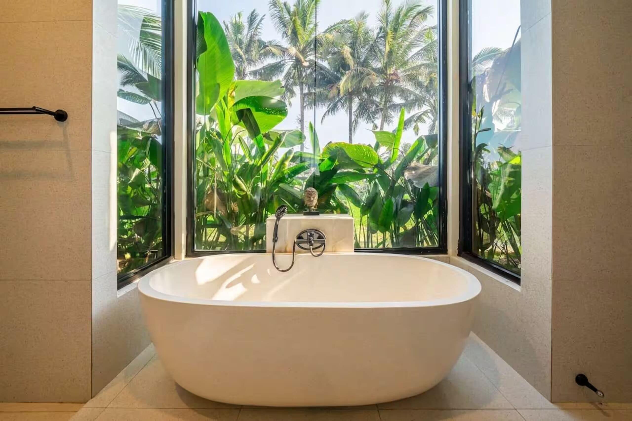 Uma banheira independente em um quarto com grandes janelas com vista para uma paisagem tropical.
