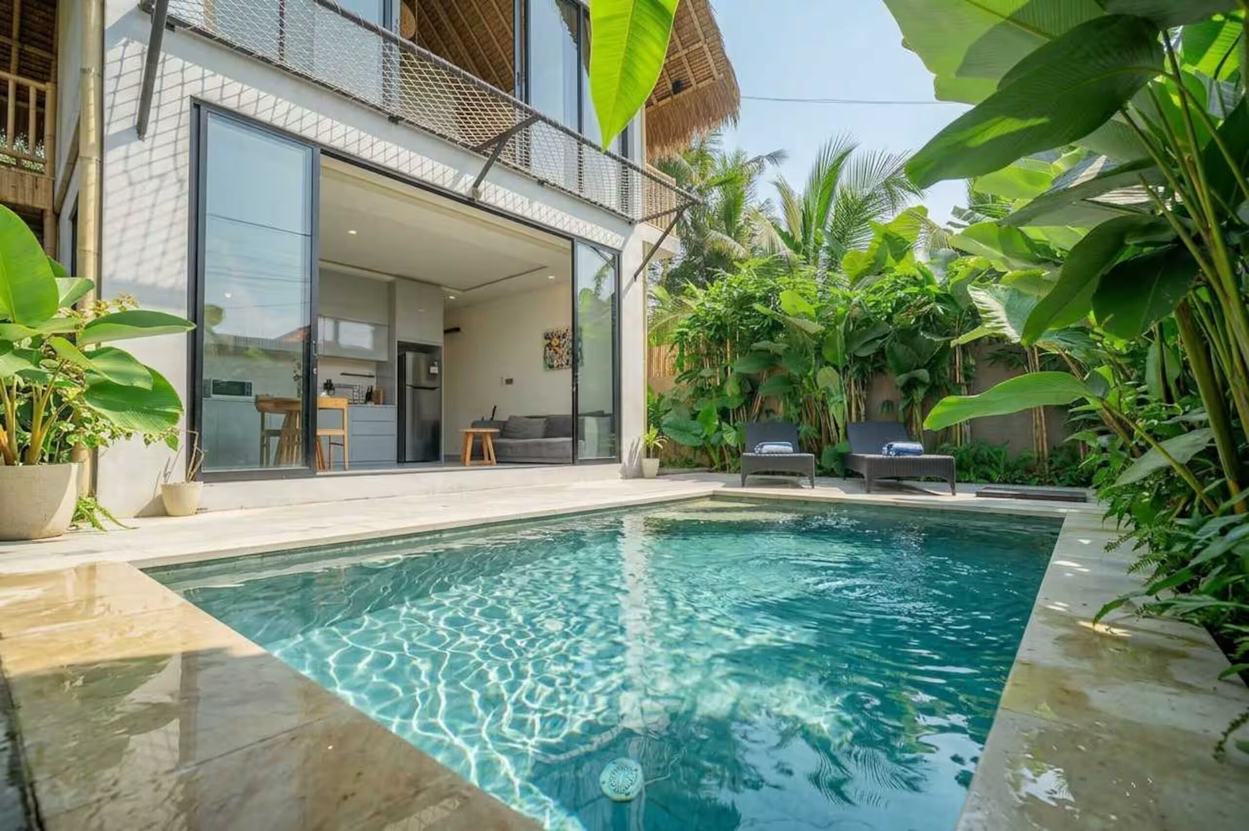 Uma casa moderna com um alpendre envidraçado, piscina e vegetação tropical exuberante.