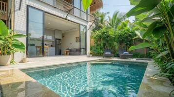Uma casa moderna com um alpendre envidraçado, piscina e vegetação tropical exuberante.