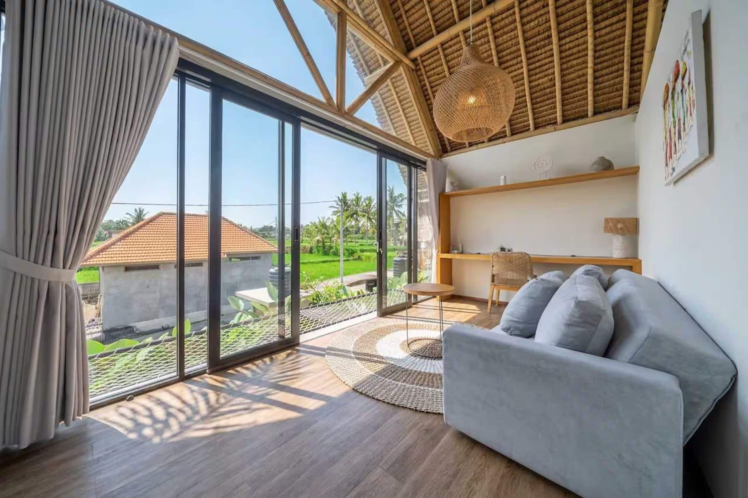 Uma sala de estar moderna com uma grande porta de vidro deslizante que dá para um jardim, um sofá, uma mesa pequena e um lustre.