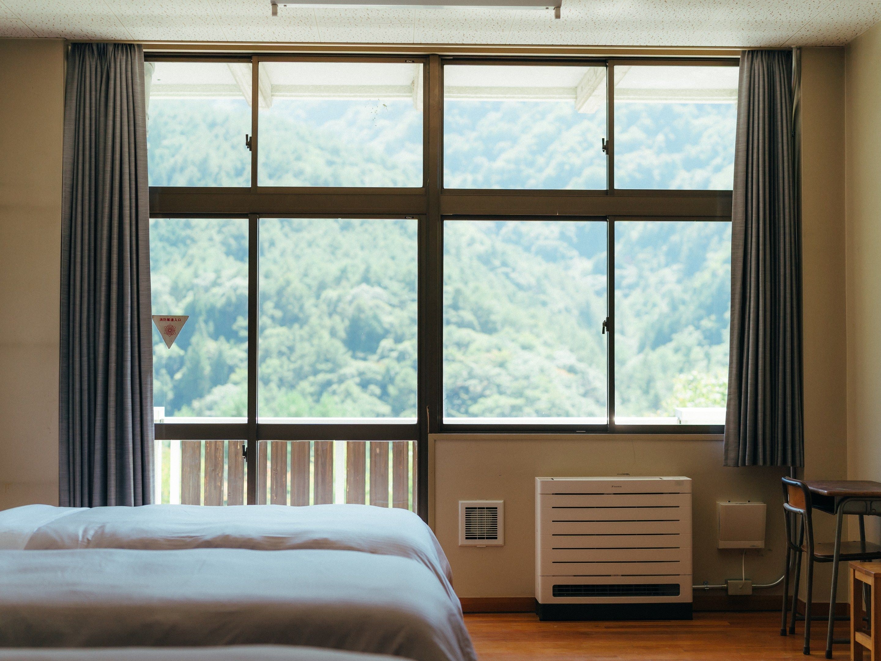 Quarto de hotel com uma janela grande, uma cama, uma escrivaninha e um ar condicionado.