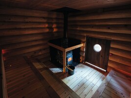 Interior de uma cabana de madeira com uma lareira a lenha no centro, uma janela e uma porta.
