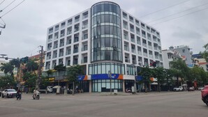 Edifício de vários andares com fachada de vidro curva, cercado por outros edifícios comerciais.