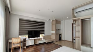 Quarto de hotel moderno com uma cama grande, escrivaninha com televisão de tela plana, armário e estantes embutidas.