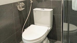 Sanitário com bidê, porta-toalhas com duas toalhas e cabine de hidromassagem em vidro.