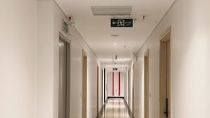 Corredor de hotel com piso brilhante, portas em ambos os lados e placas de sinalização no teto.