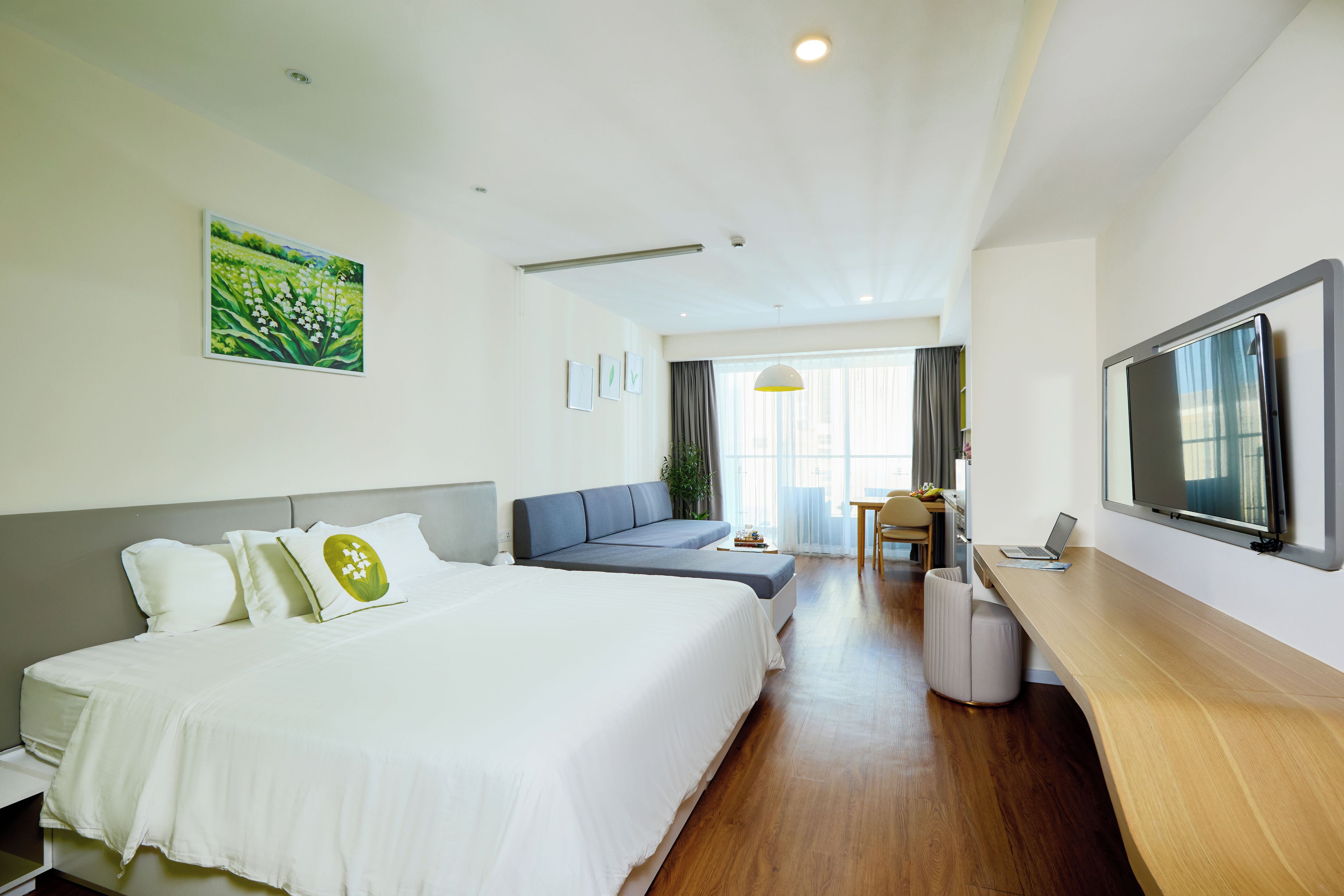 Quarto de hotel com cama, sofá, escrivaninha com laptop, televisão e pintura na parede.