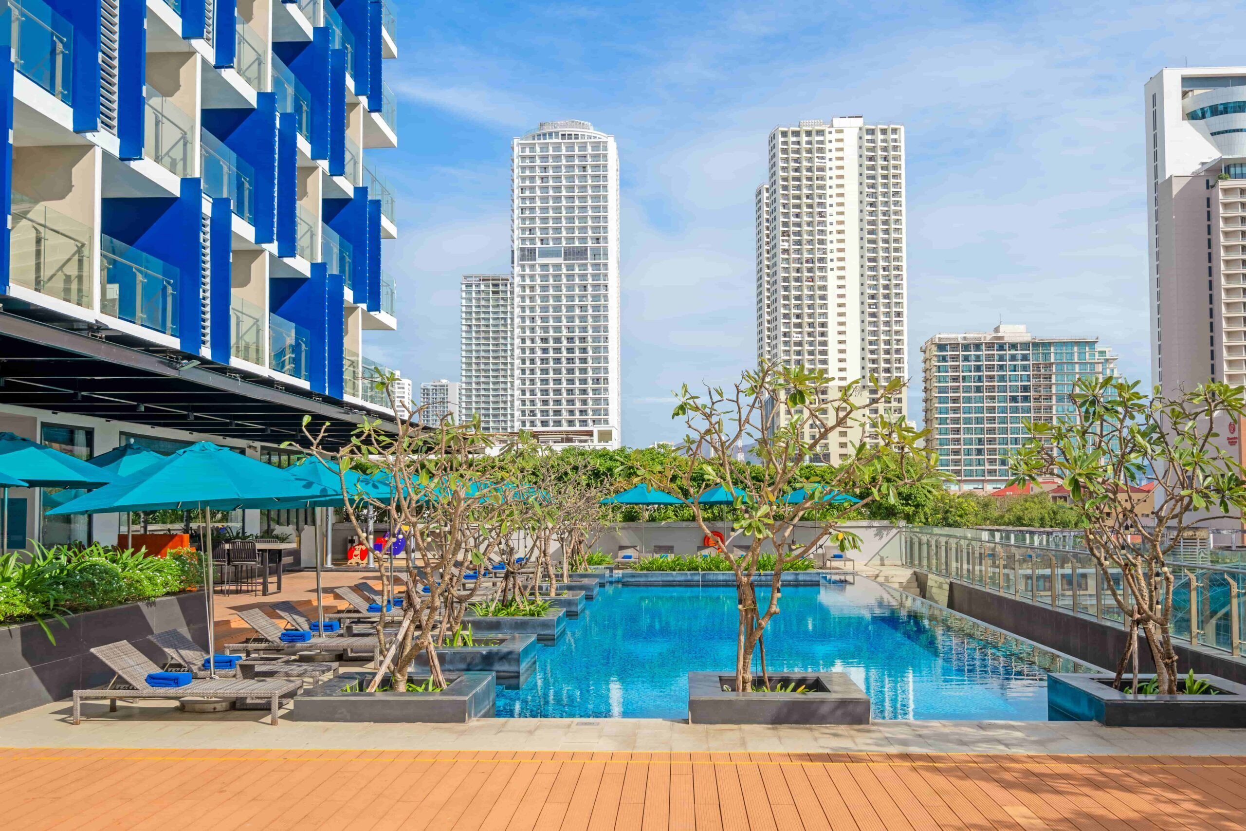 Piscina no terraço com espreguiçadeiras e guarda-sóis, rodeada por edifícios residenciais altos.