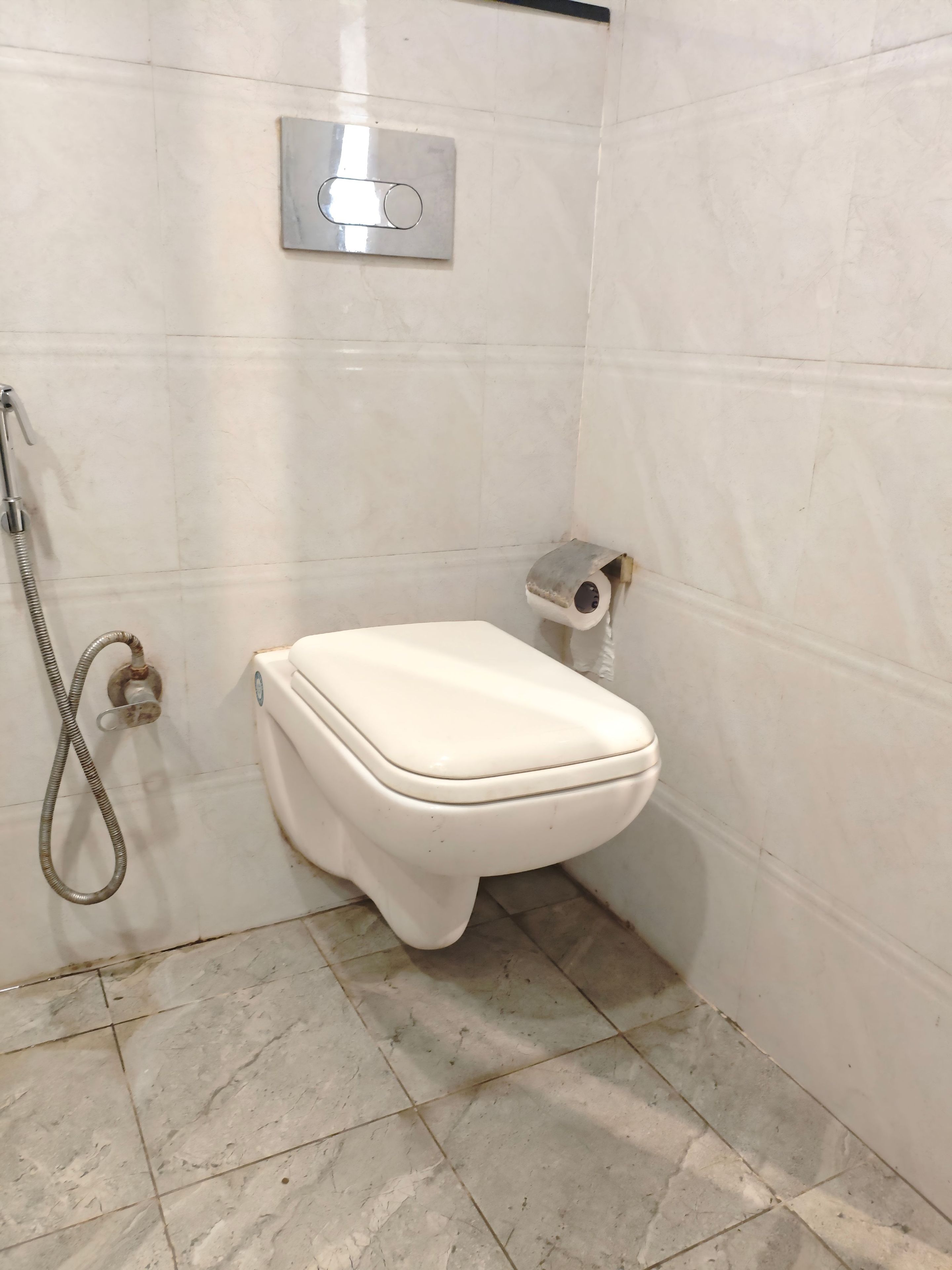 Um banheiro pequeno e revestido com azulejos, com vaso sanitário, chuveiro e suporte para papel higiênico.