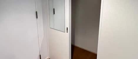 Quarto com piso de madeira, porta branca e armário com espaço para pendurar roupas.