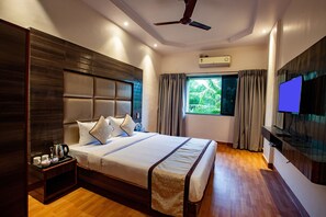Quarto de hotel com uma cama grande, televisão, ventoinha no teto e janela com cortinas.